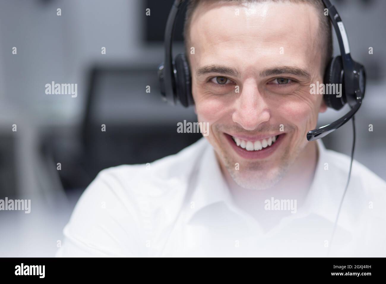young smiling male call centre operator doing his job with a headset ...