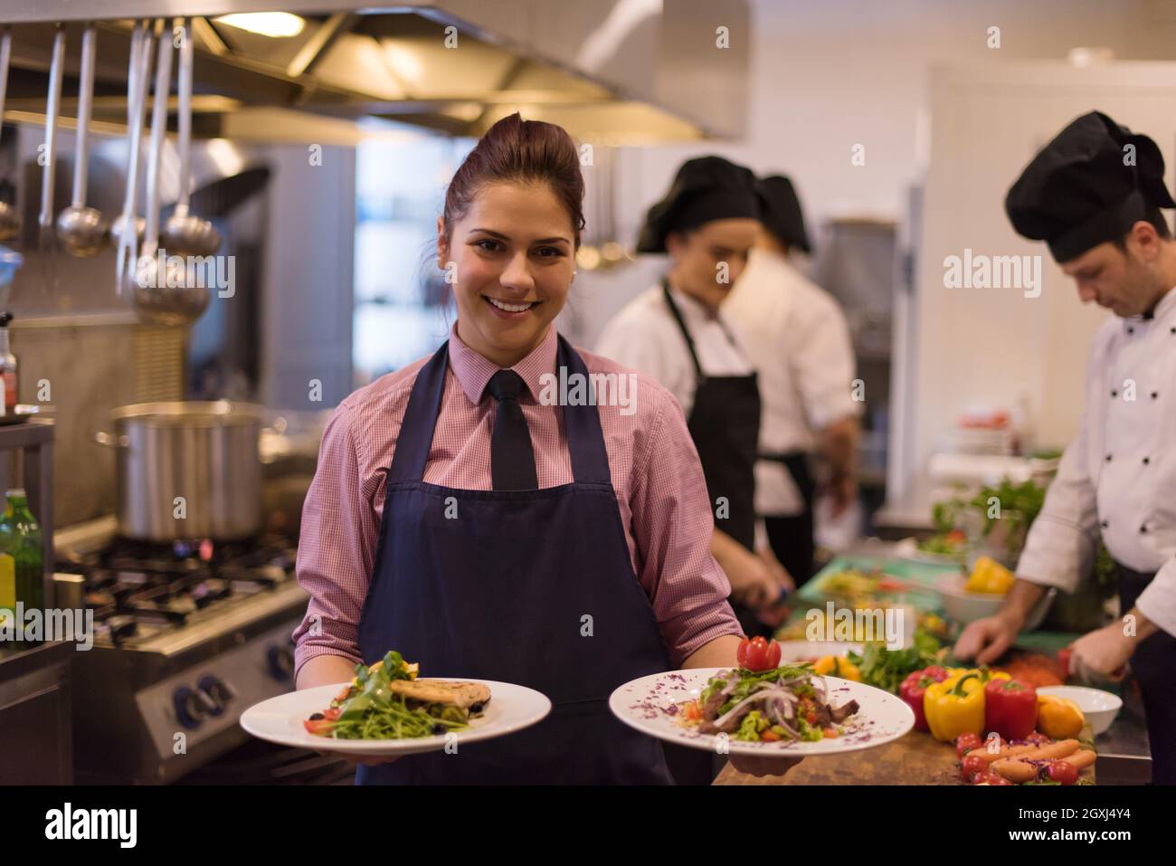 young waitress presenting dishes of tasty meals in commercial kitchen ...