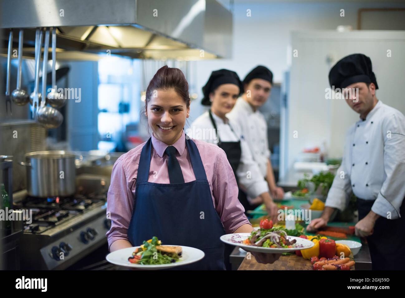 young waitress presenting dishes of tasty meals in commercial kitchen ...
