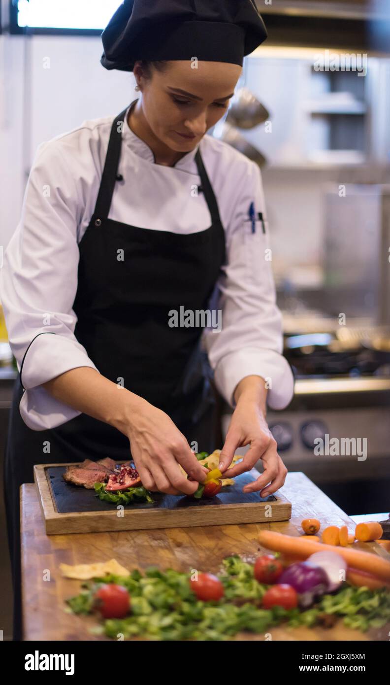 female Chef in hotel or restaurant kitchen preparing beef steak with ...
