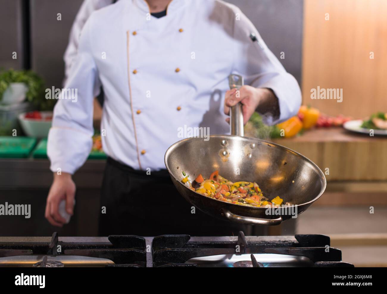 Young male chef flipping vegetables in wok at commercial kitchen Stock ...
