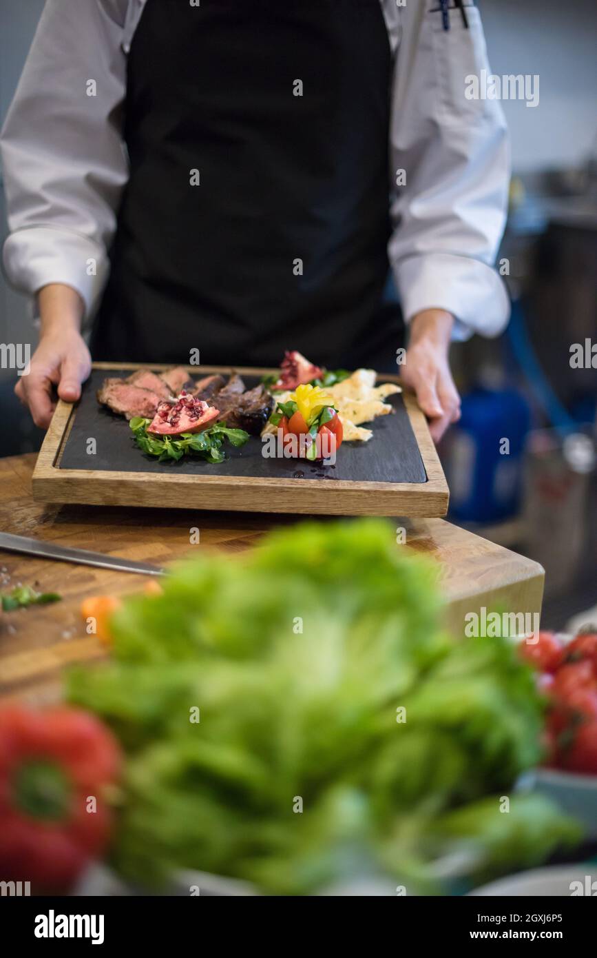 female Chef in hotel or restaurant kitchen holding grilled beef steak ...