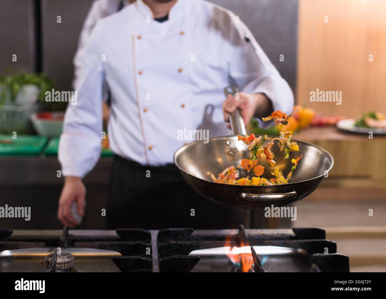 Young male chef flipping vegetables in wok at commercial kitchen Stock ...