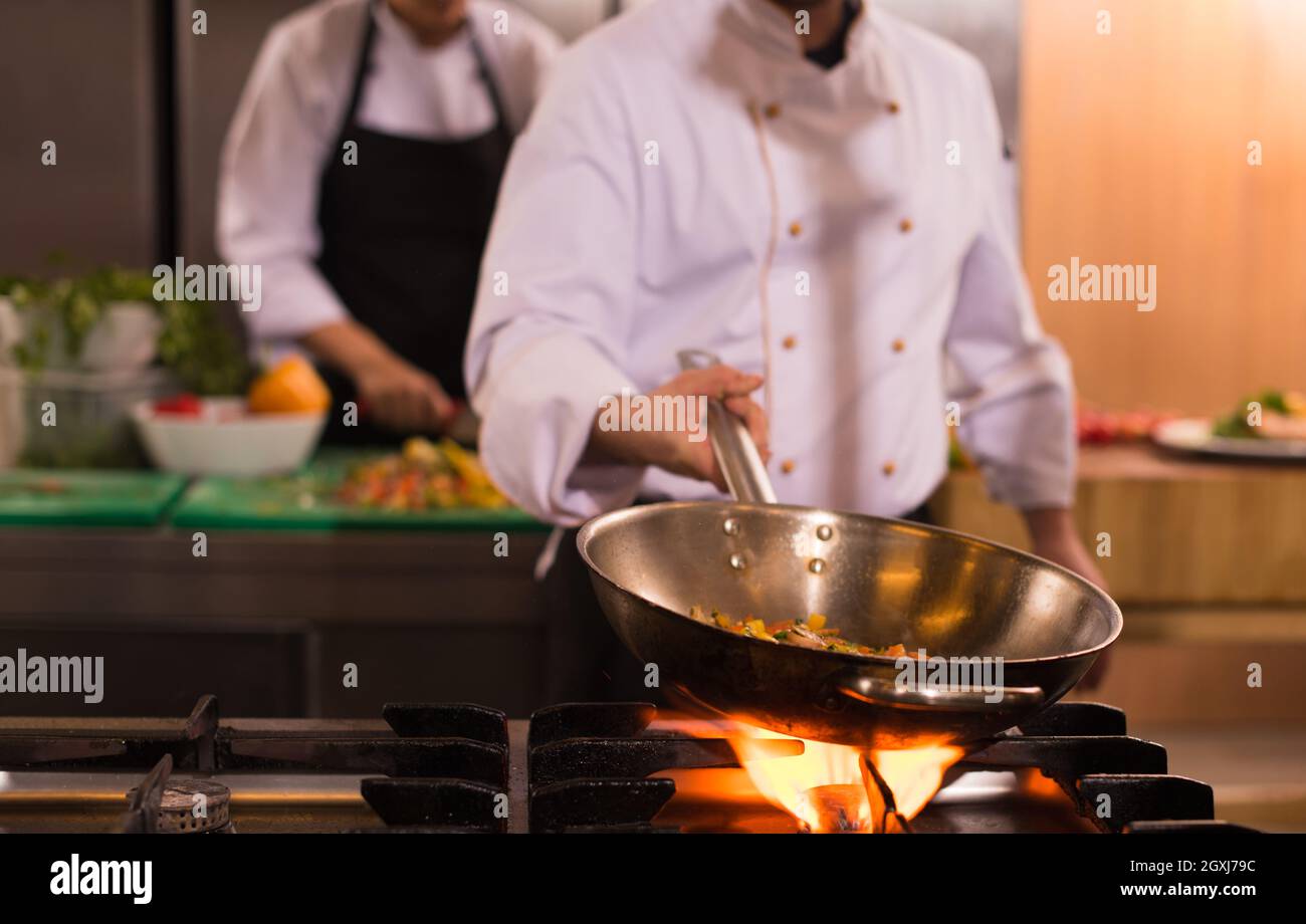 Young male chef flipping vegetables in wok at commercial kitchen Stock ...