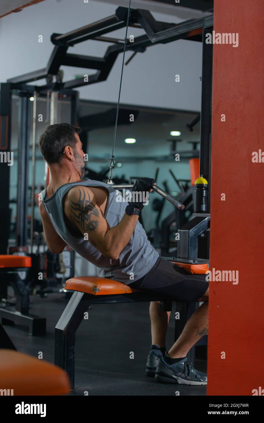 Strong 50 year old man exercising lat pushdown at the cable machine in ...
