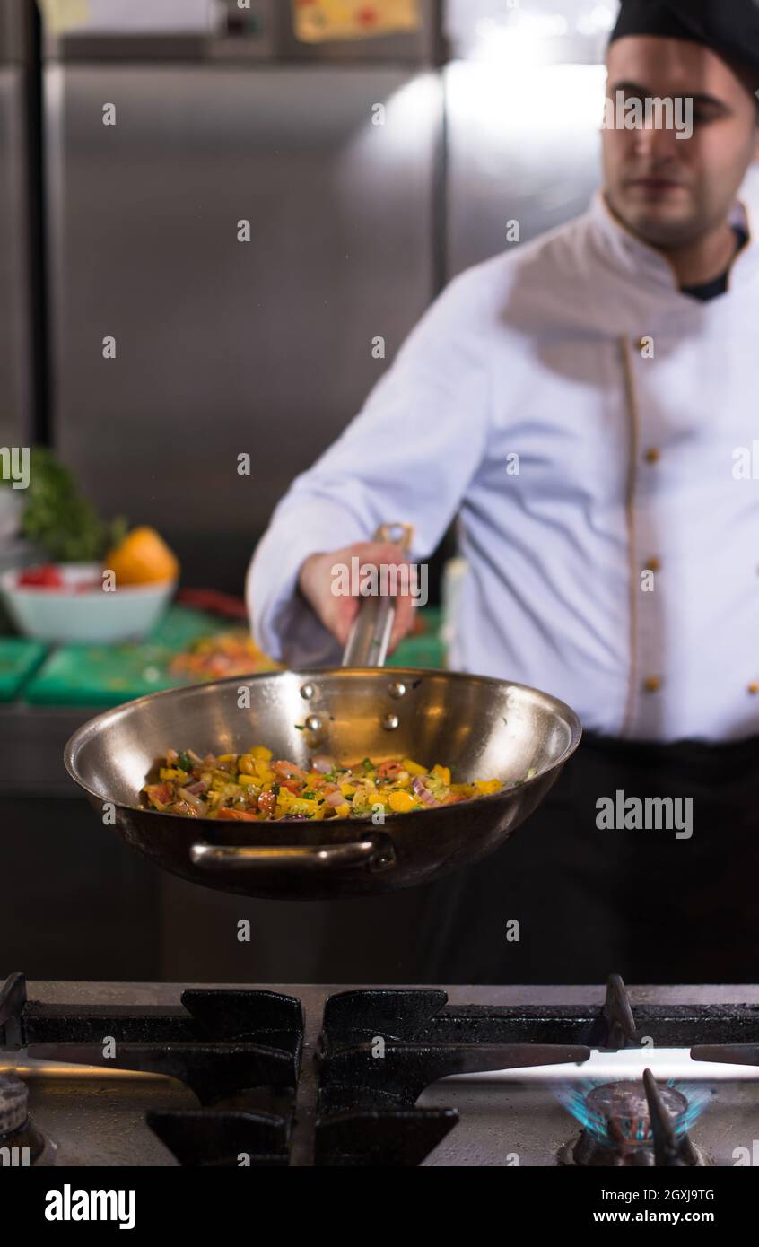 Young male chef flipping vegetables in wok at commercial kitchen Stock ...