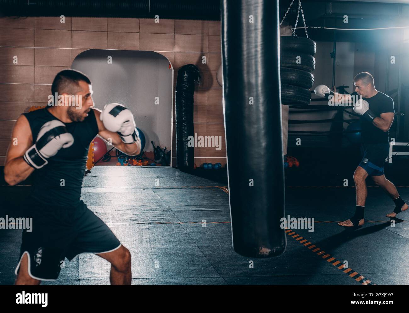 Strong kickboxer man punching black sand bag on gym background Stock ...