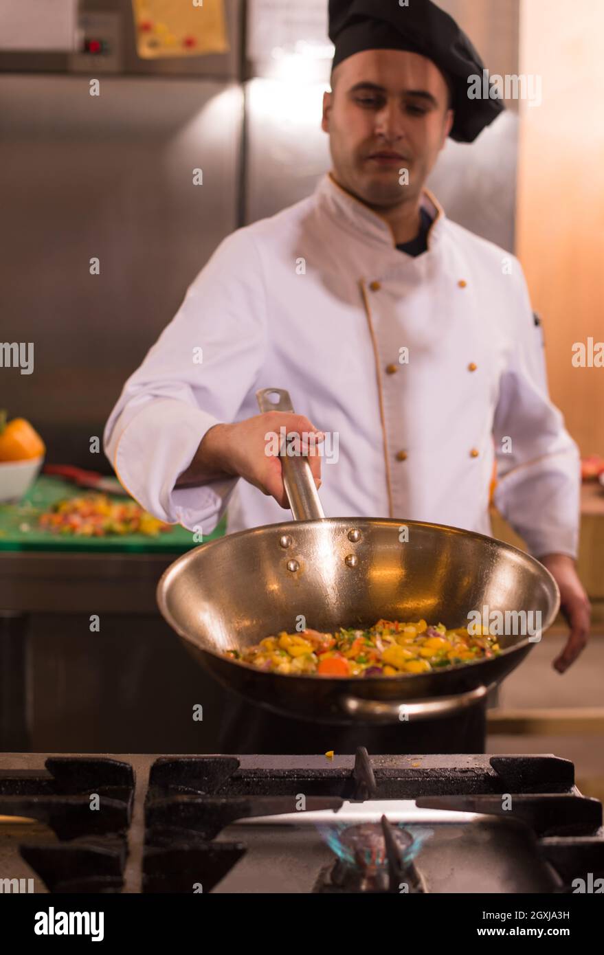 Young male chef flipping vegetables in wok at commercial kitchen Stock ...
