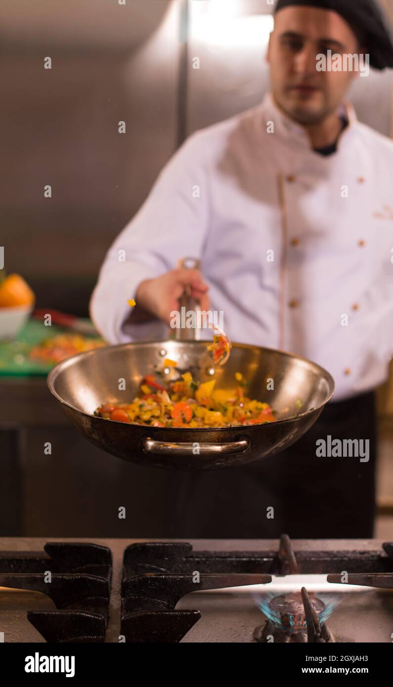 Young male chef flipping vegetables in wok at commercial kitchen Stock ...