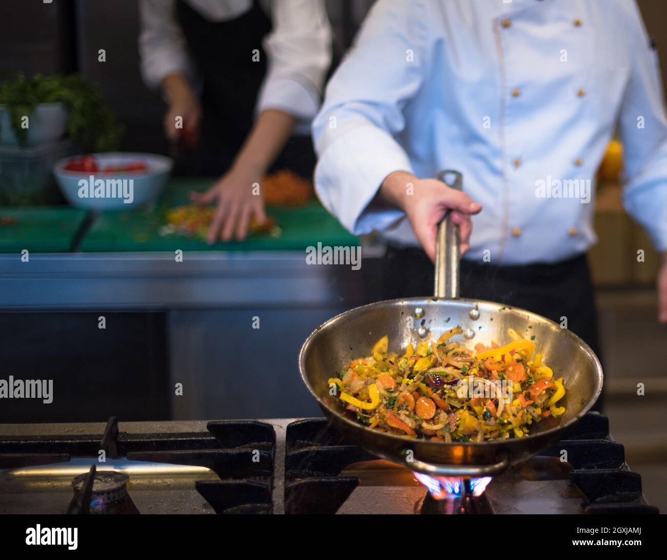 Young male chef flipping vegetables in wok at commercial kitchen Stock ...
