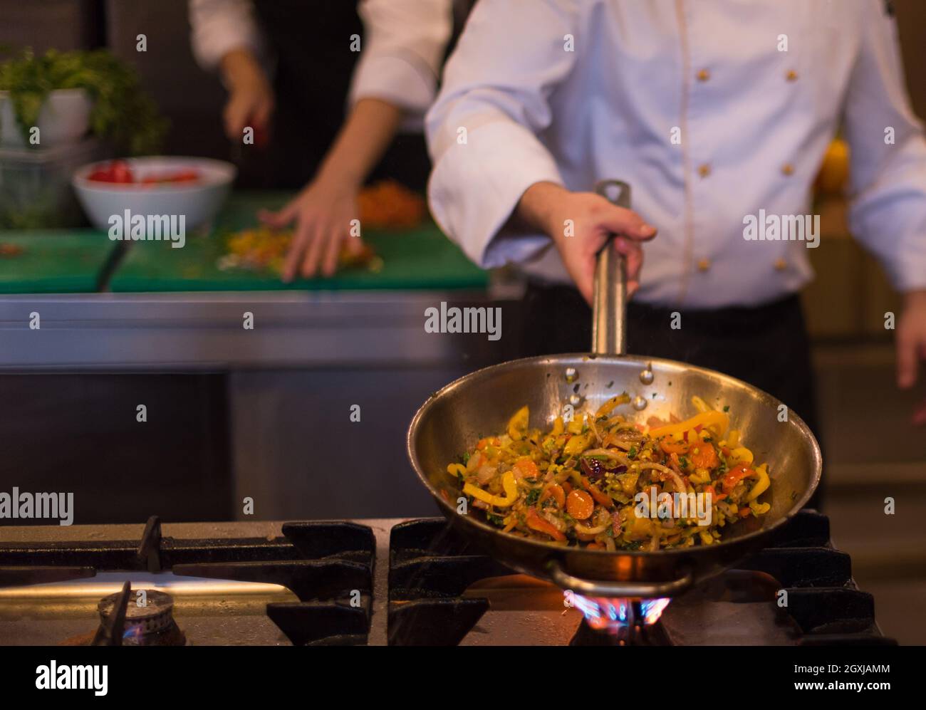 Young male chef flipping vegetables in wok at commercial kitchen Stock ...