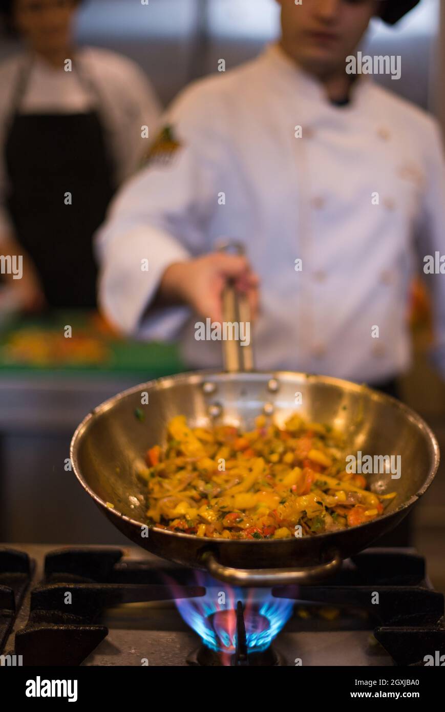 Young male chef flipping vegetables in wok at commercial kitchen Stock ...