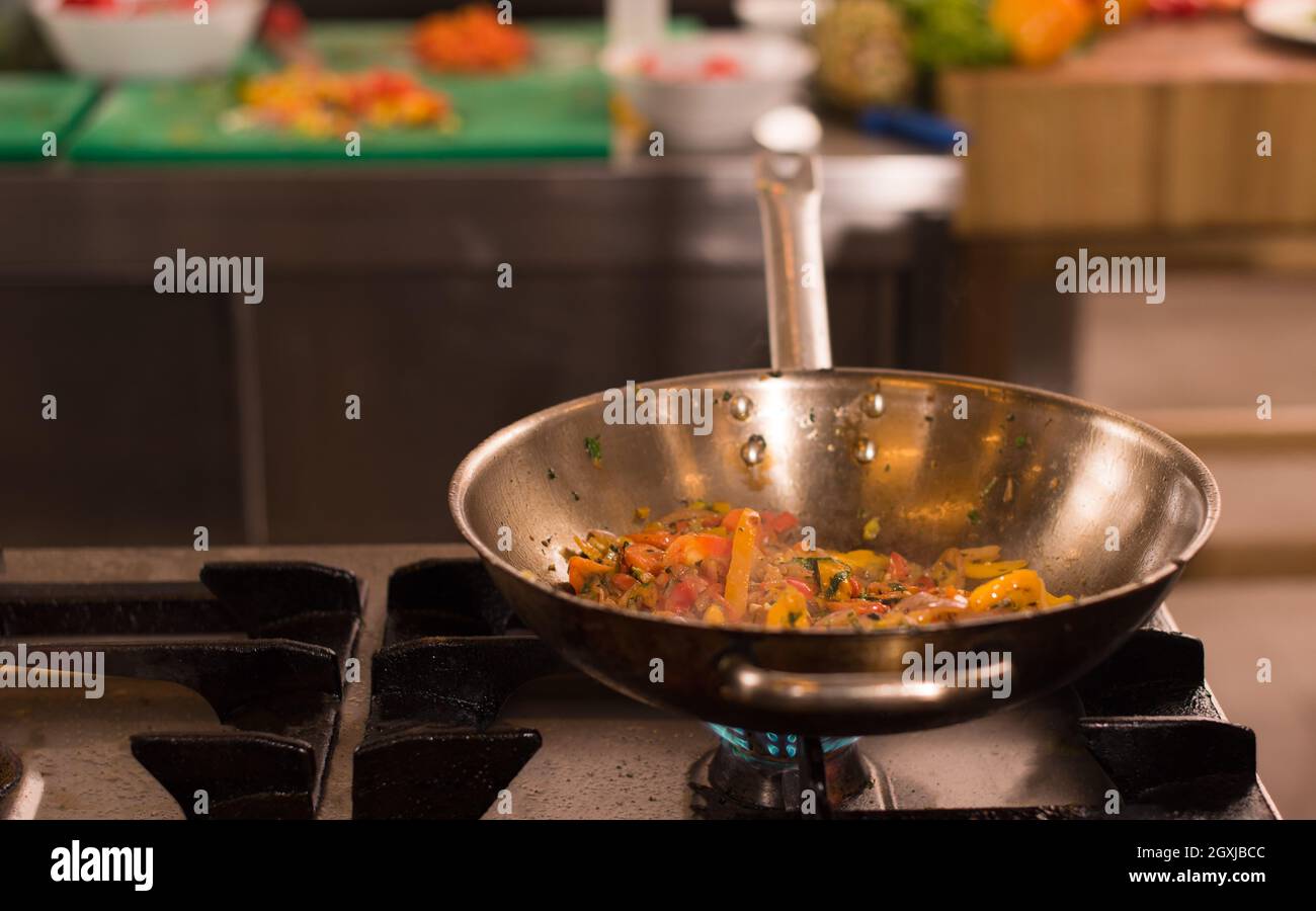 Young male chef flipping vegetables in wok at commercial kitchen Stock ...