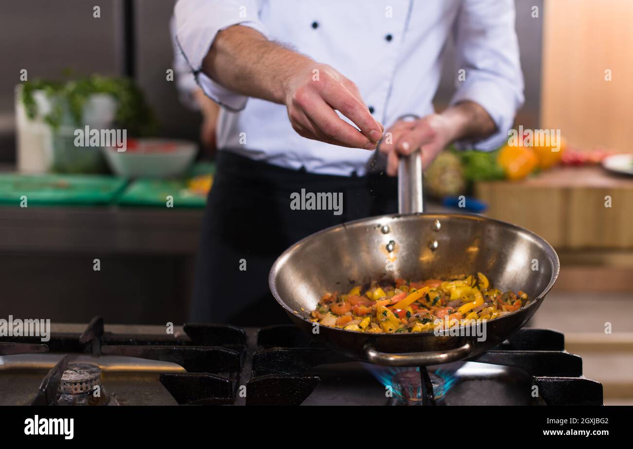 Young male chef putting spices on vegetables in wok at commercial ...