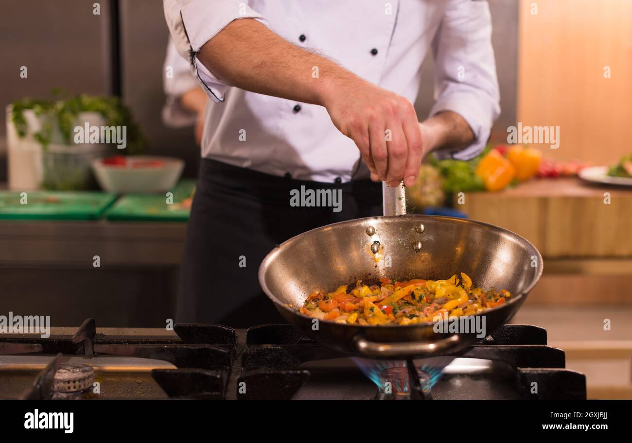 Young male chef putting spices on vegetables in wok at commercial ...
