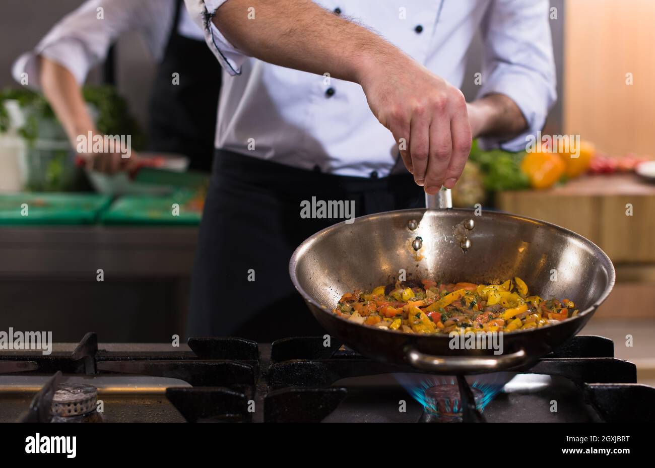 Young male chef putting spices on vegetables in wok at commercial ...