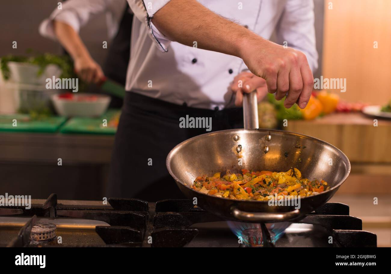 Young male chef putting spices on vegetables in wok at commercial ...