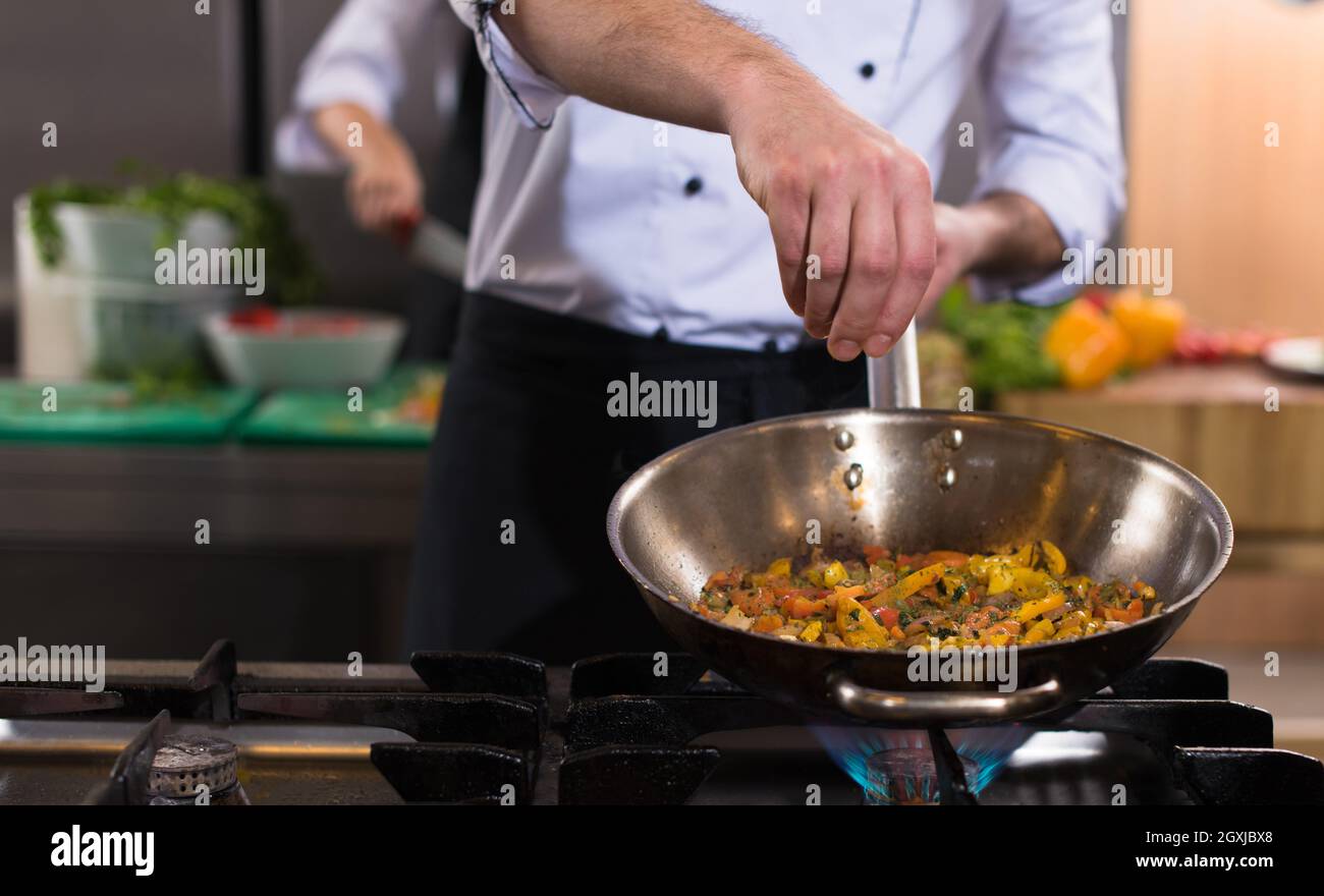 Young male chef putting spices on vegetables in wok at commercial ...