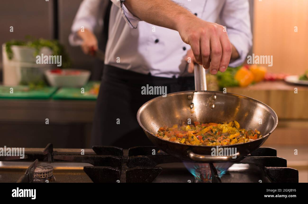 Young male chef putting spices on vegetables in wok at commercial ...