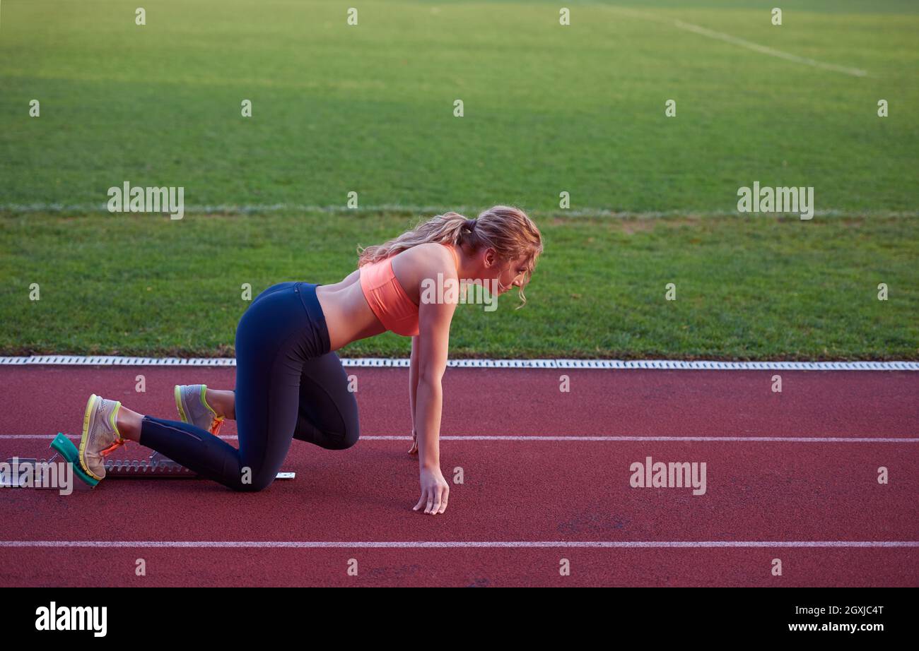 woman sprinter leaving starting blocks on the athletic track. Side view ...