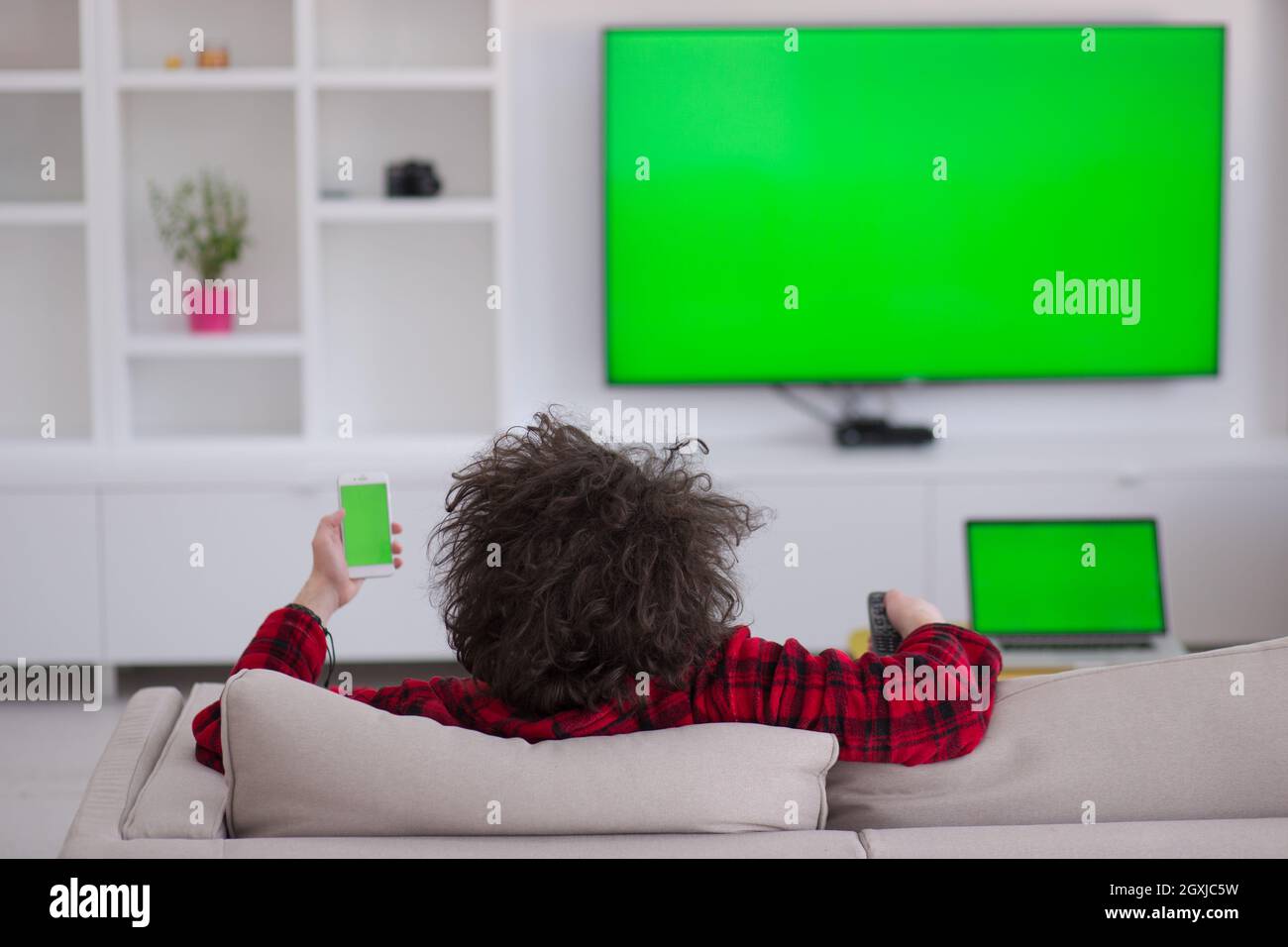 young handsome man in bathrobe enjoying free time watching television ...