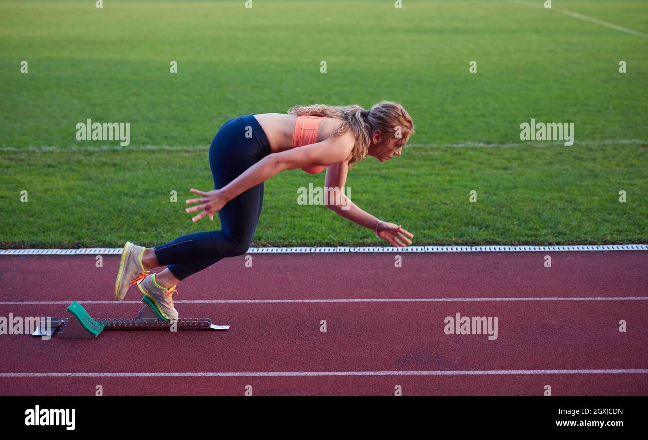 woman sprinter leaving starting blocks on the athletic track. Side view ...