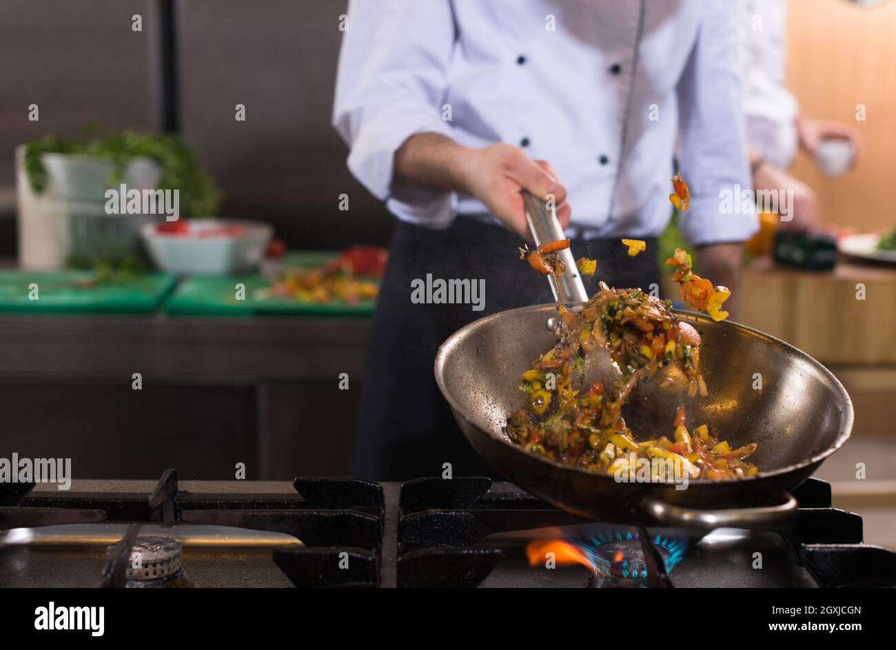 Young male chef flipping vegetables in wok at commercial kitchen Stock ...
