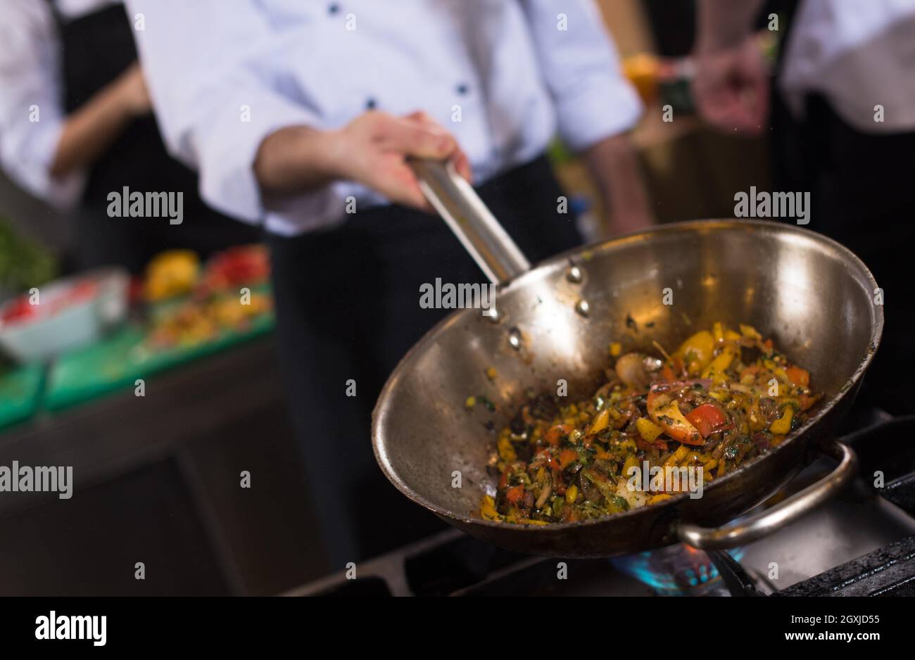 Young male chef flipping vegetables in wok at commercial kitchen Stock ...