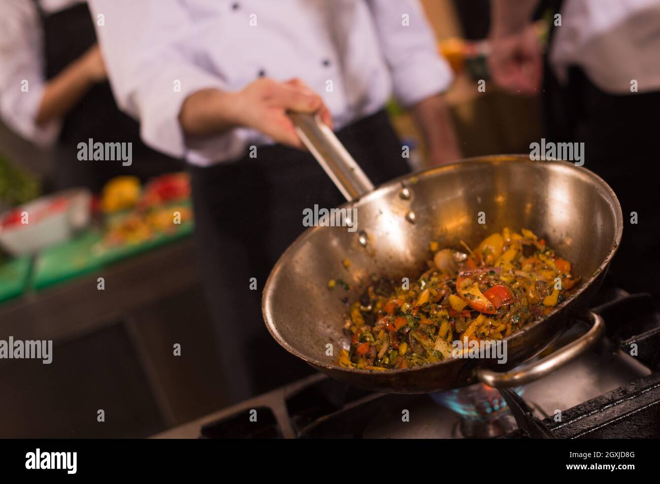 Young male chef flipping vegetables in wok at commercial kitchen Stock ...