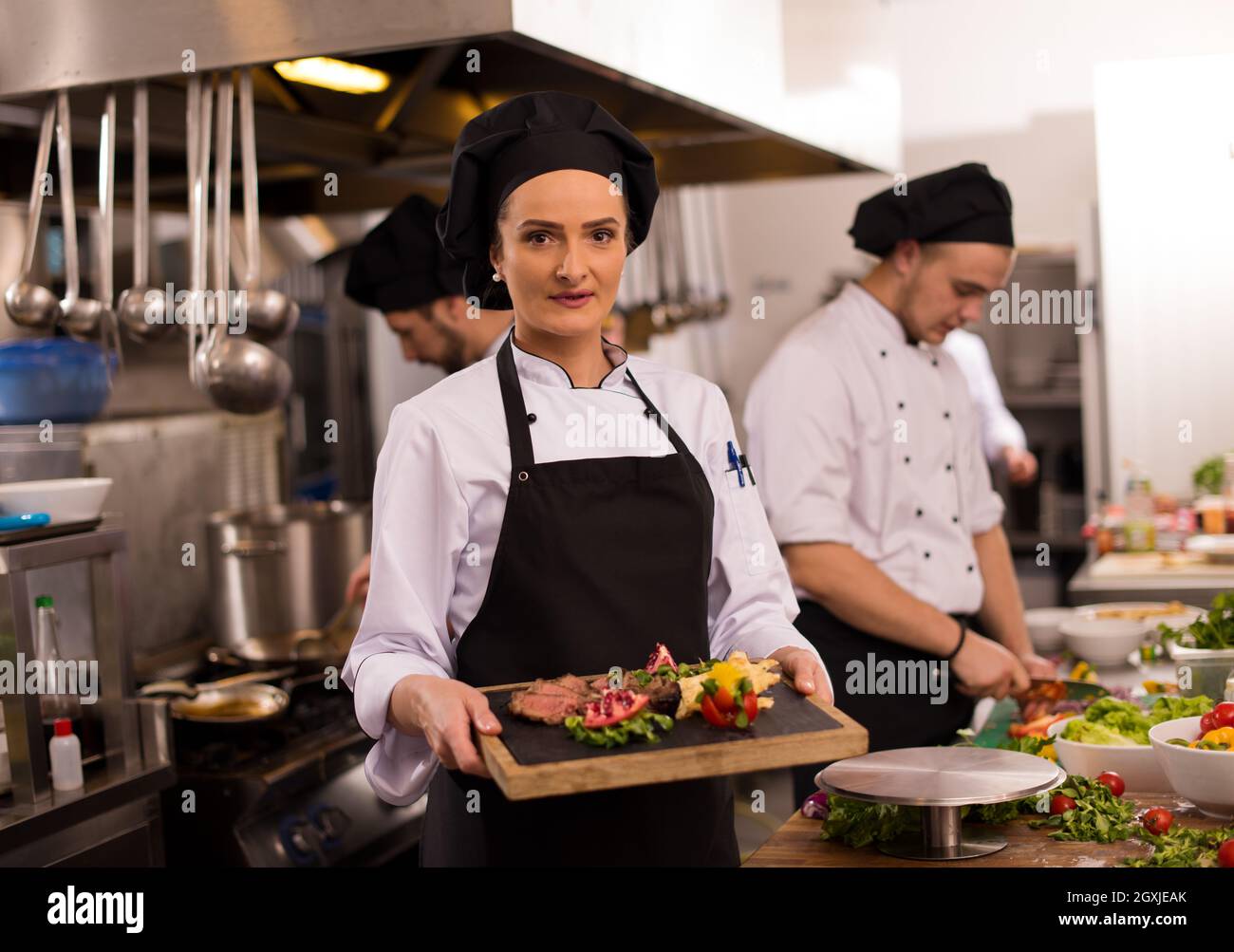 female Chef in hotel or restaurant kitchen holding grilled beef steak ...
