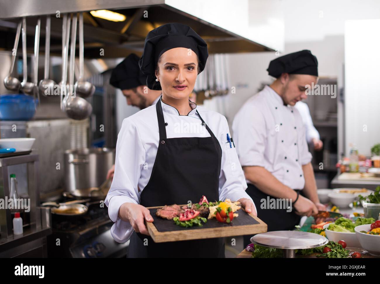 female Chef in hotel or restaurant kitchen holding grilled beef steak ...