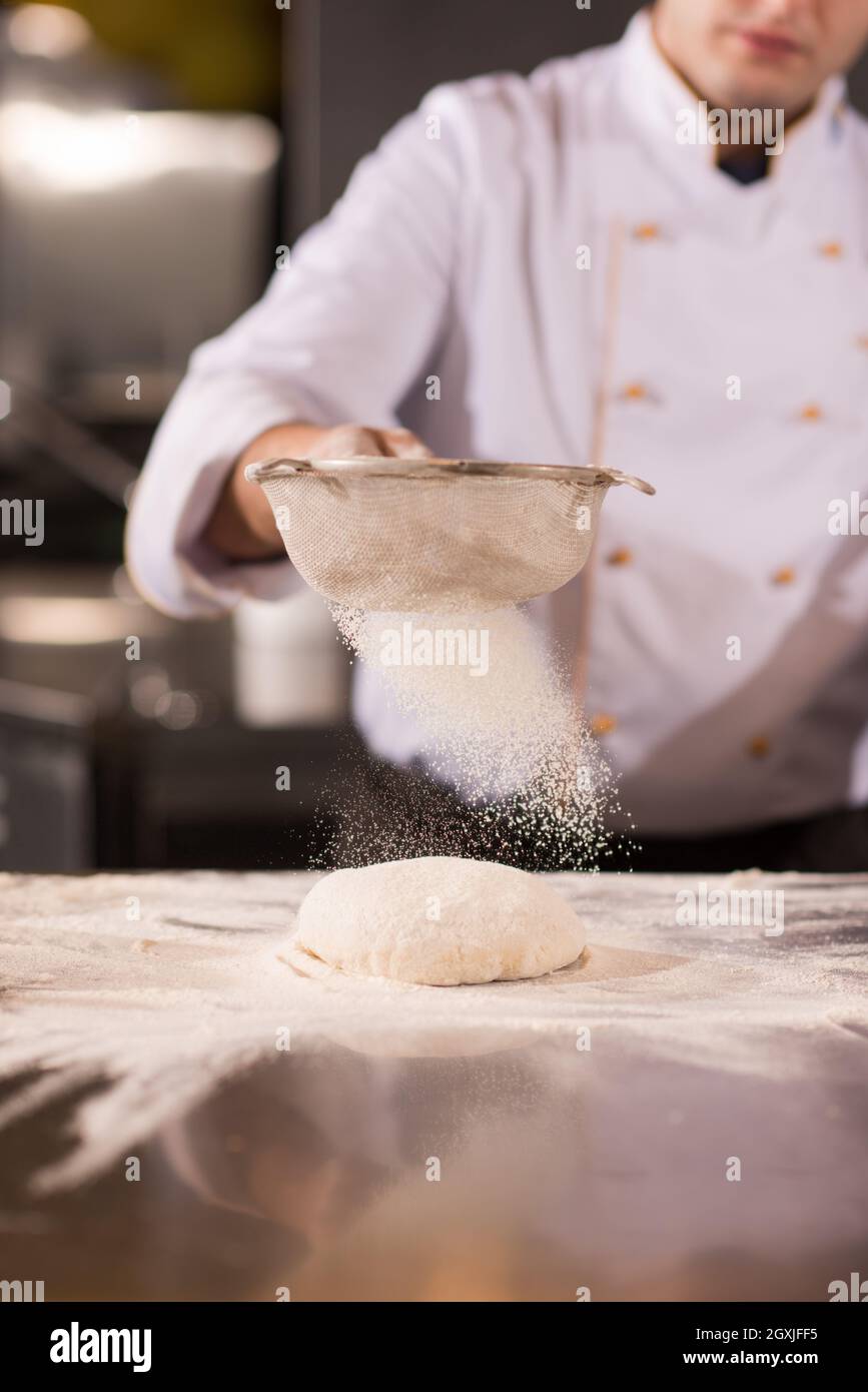 chef sprinkling flour over fresh pizza dough on kitchen table Stock ...