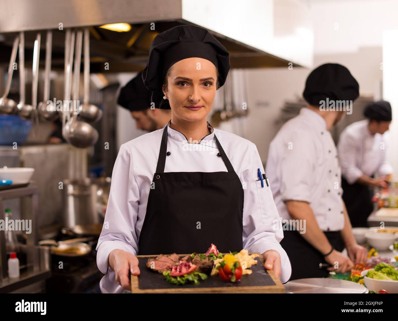 female Chef in hotel or restaurant kitchen holding grilled beef steak ...
