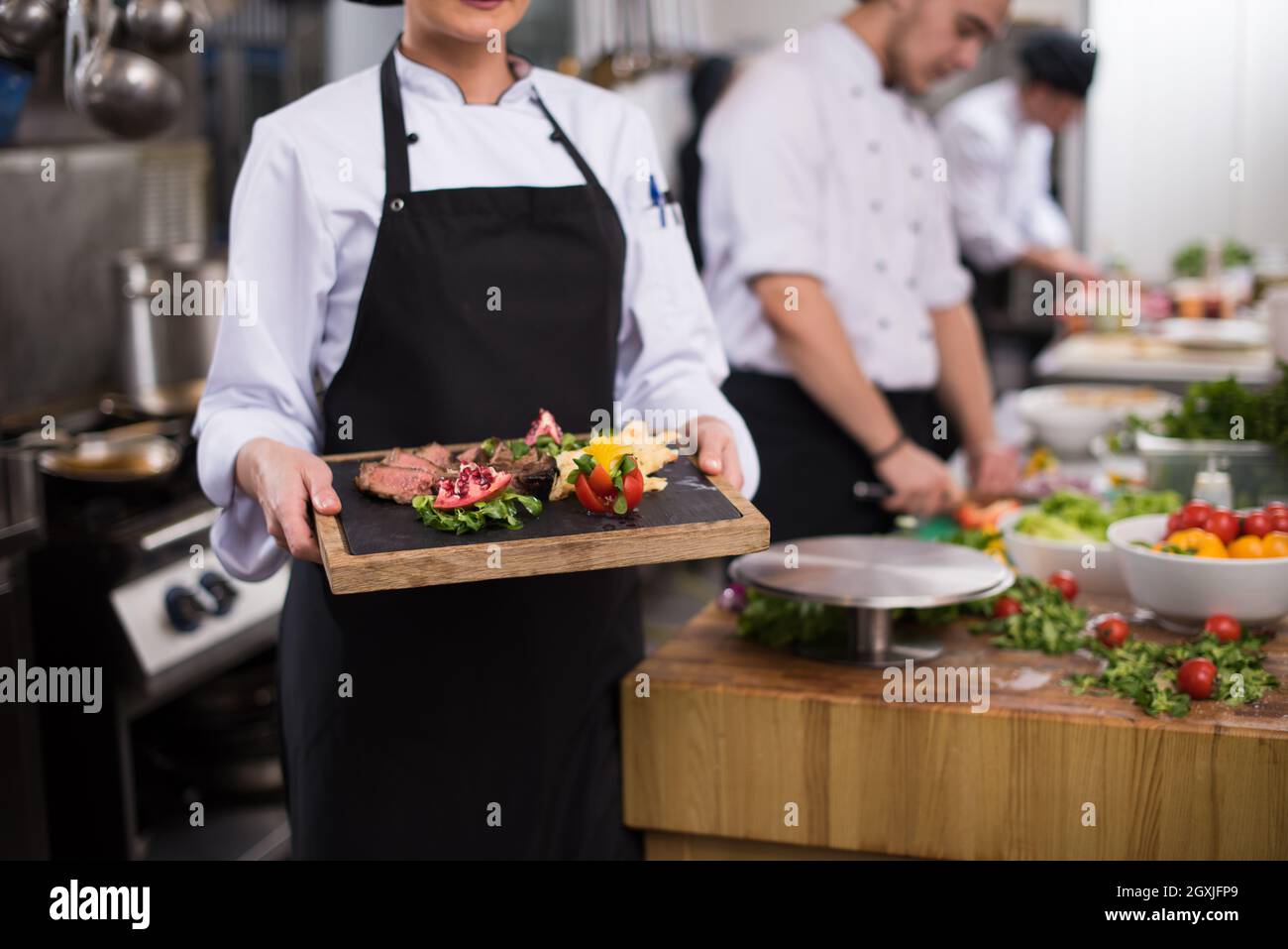 female Chef in hotel or restaurant kitchen holding grilled beef steak ...