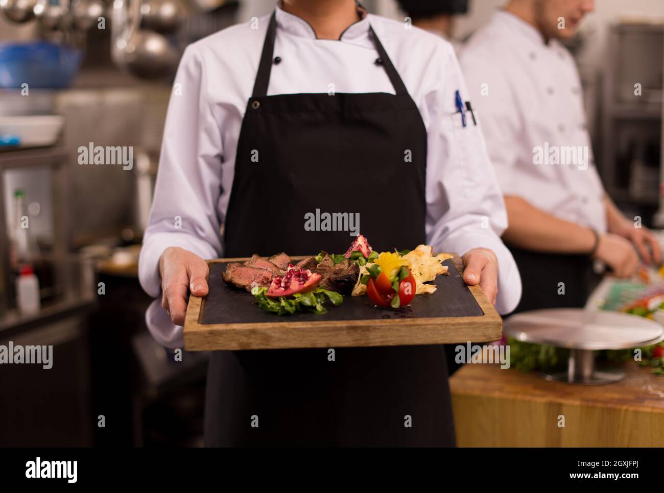 female Chef in hotel or restaurant kitchen holding grilled beef steak ...