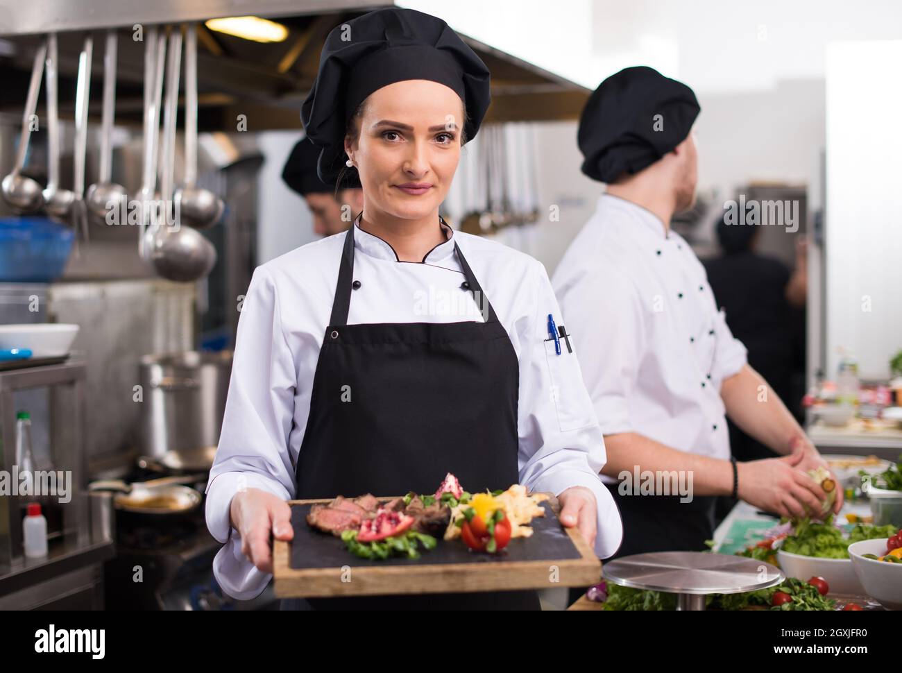 female Chef in hotel or restaurant kitchen holding grilled beef steak ...