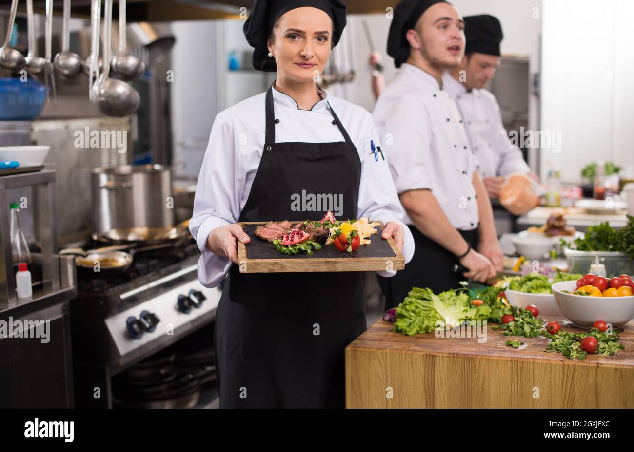 female Chef in hotel or restaurant kitchen holding grilled beef steak ...
