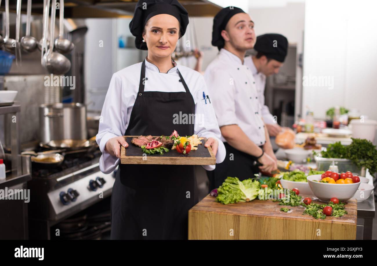 female Chef in hotel or restaurant kitchen holding grilled beef steak ...