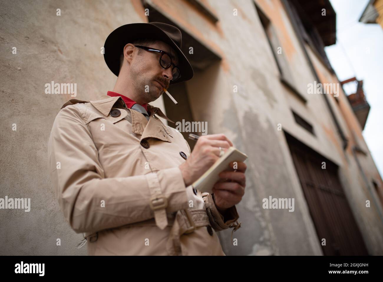 Detective writing on a notebook while standing against an old wall ...