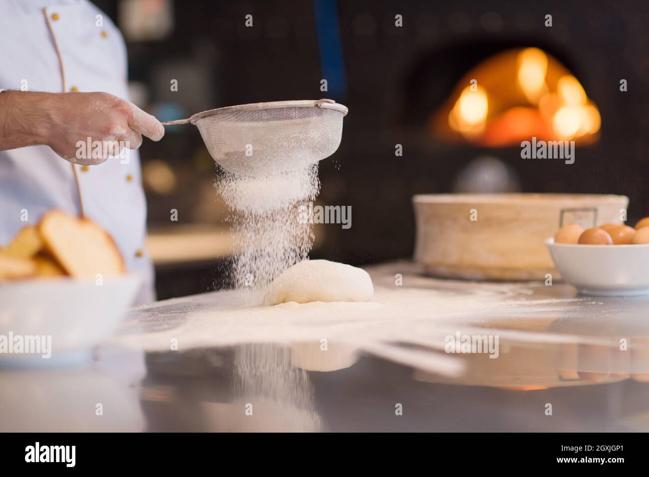 chef sprinkling flour over fresh pizza dough on kitchen table Stock ...