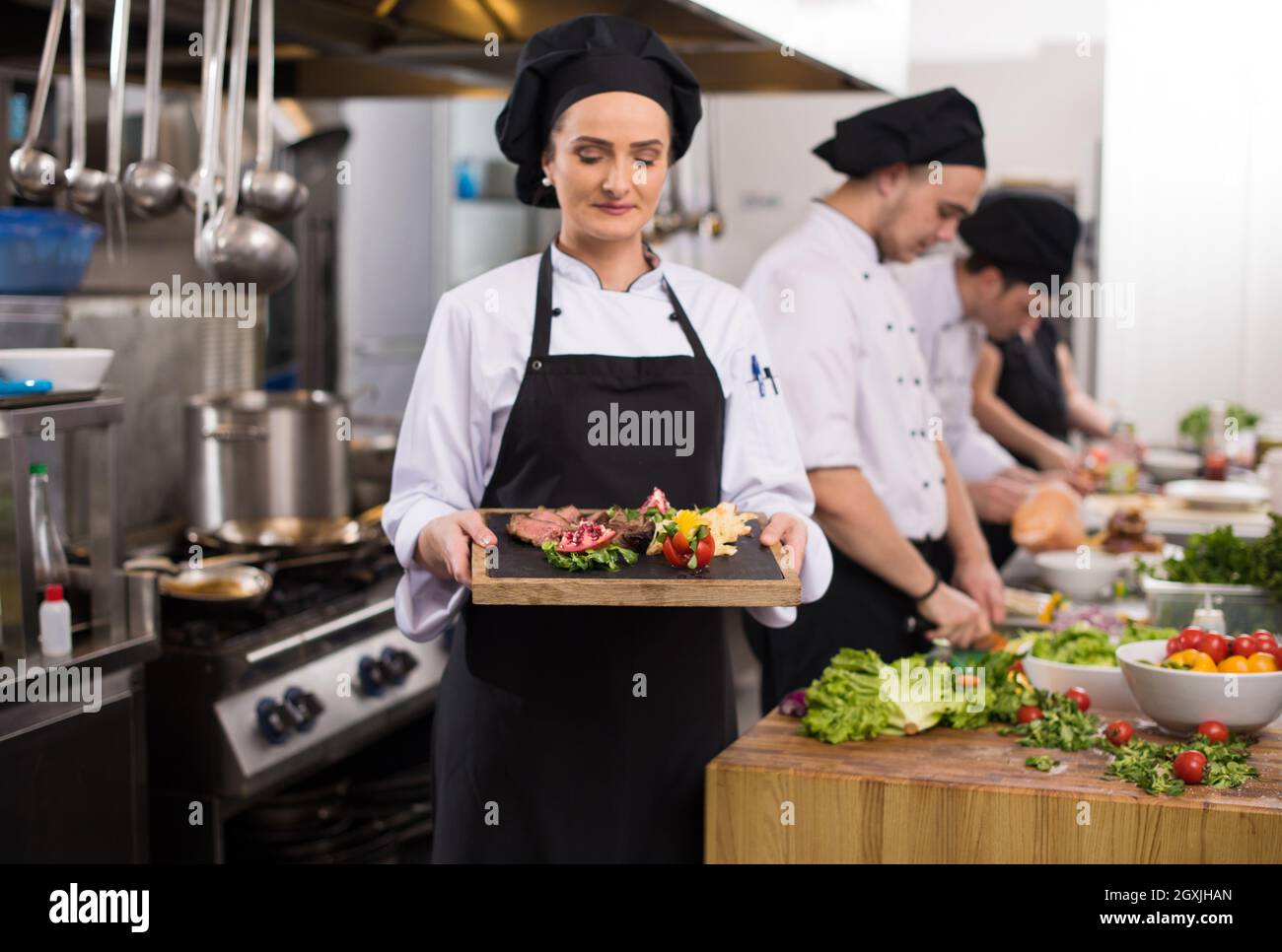 female Chef in hotel or restaurant kitchen holding grilled beef steak ...