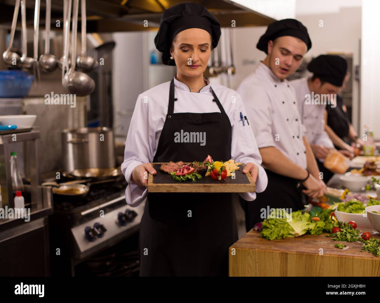 female Chef in hotel or restaurant kitchen holding grilled beef steak ...