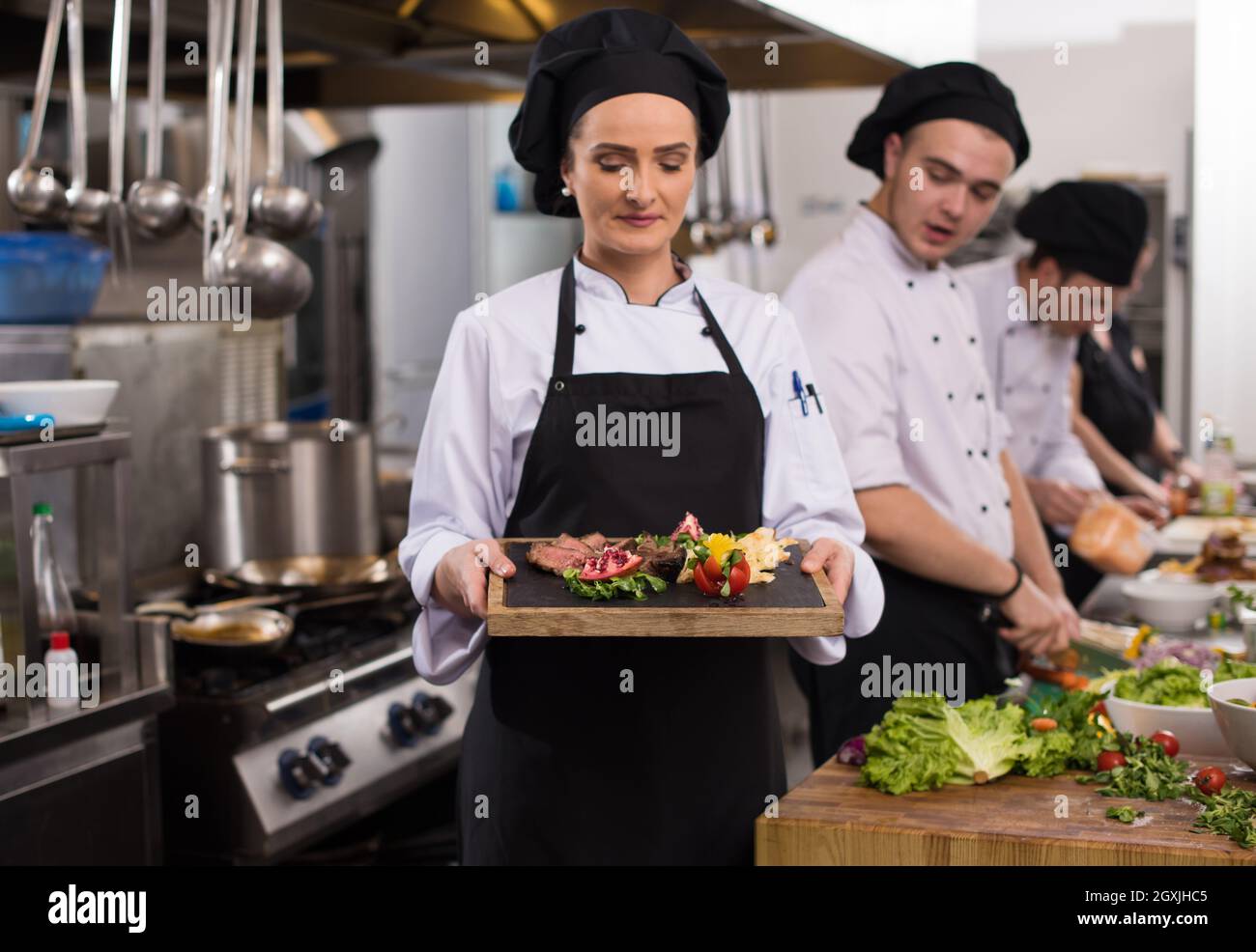 female Chef in hotel or restaurant kitchen holding grilled beef steak ...