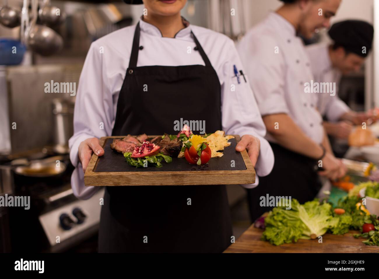 female Chef in hotel or restaurant kitchen holding grilled beef steak ...