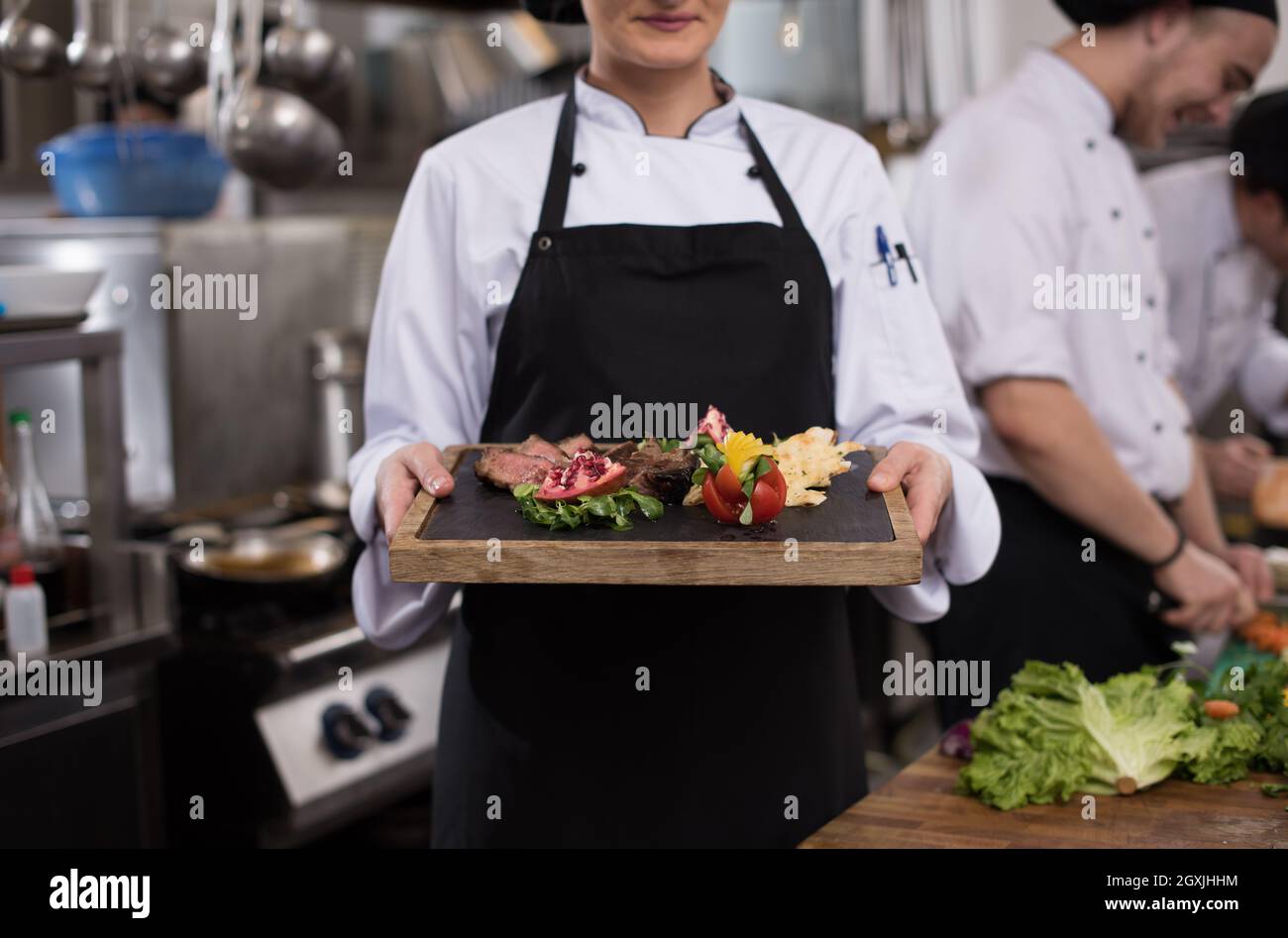 female Chef in hotel or restaurant kitchen holding grilled beef steak ...