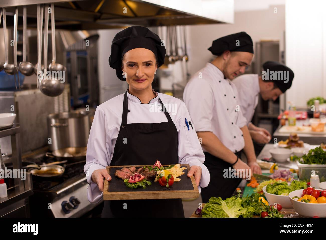 female Chef in hotel or restaurant kitchen holding grilled beef steak ...