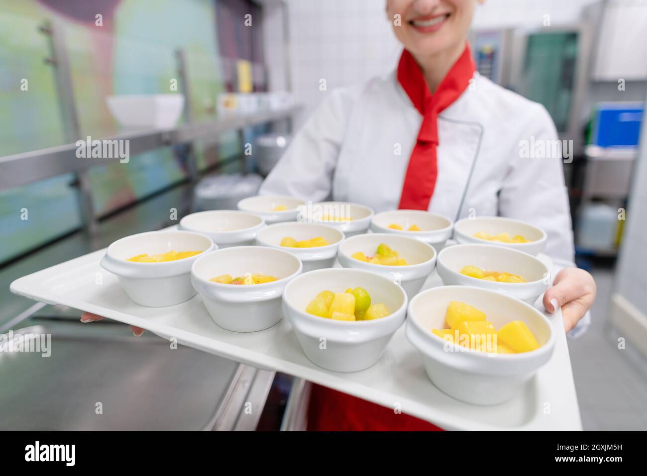 Cook in commercial kitchen showing tray with dessert ready to be served ...