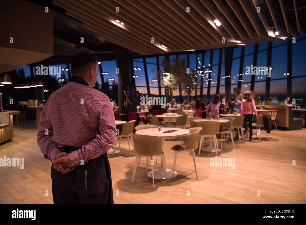 Rear view of young confident waiter standing with hands behind his back ...