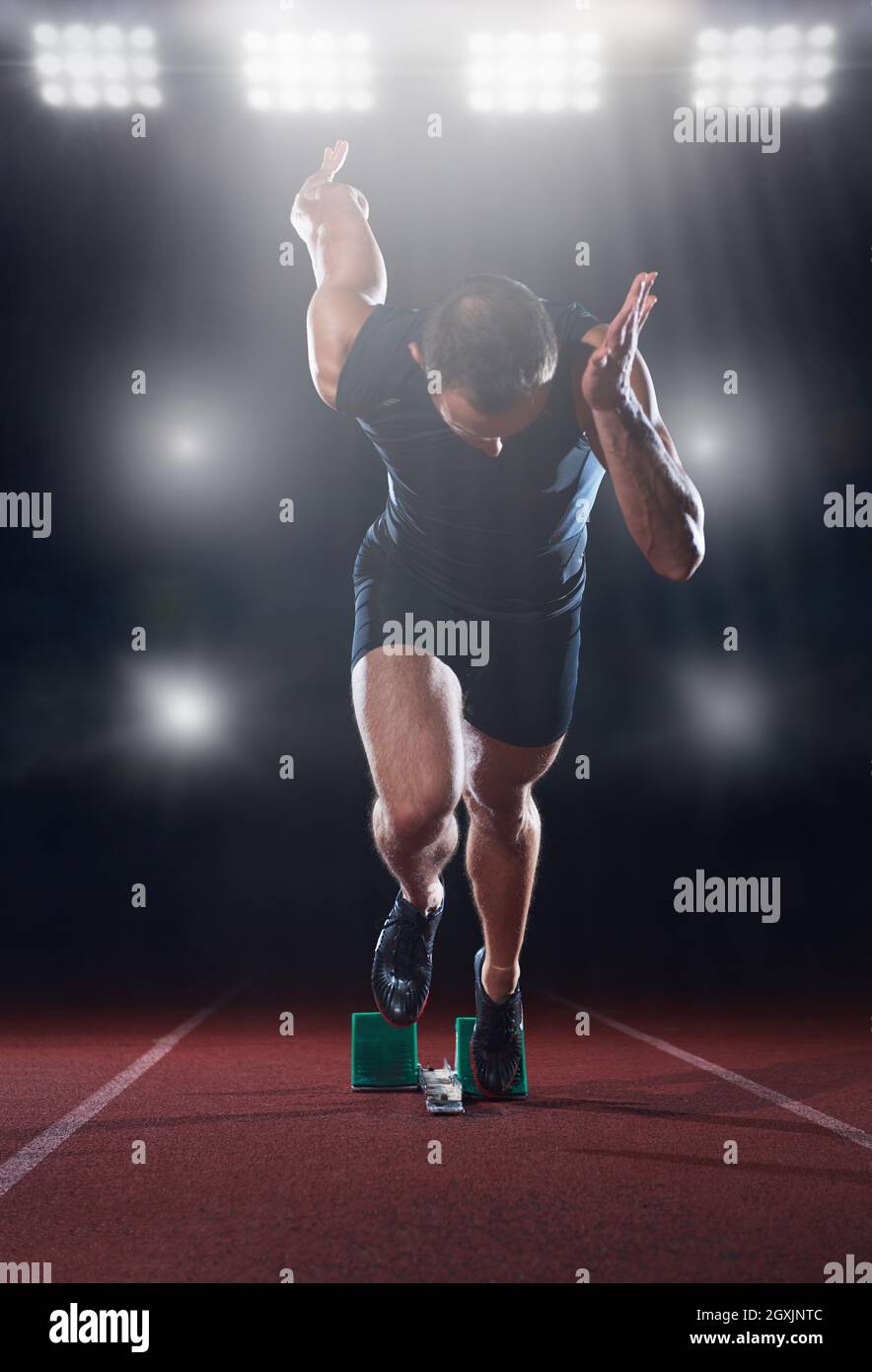 Sprinter leaving starting blocks on the running track in front of big ...