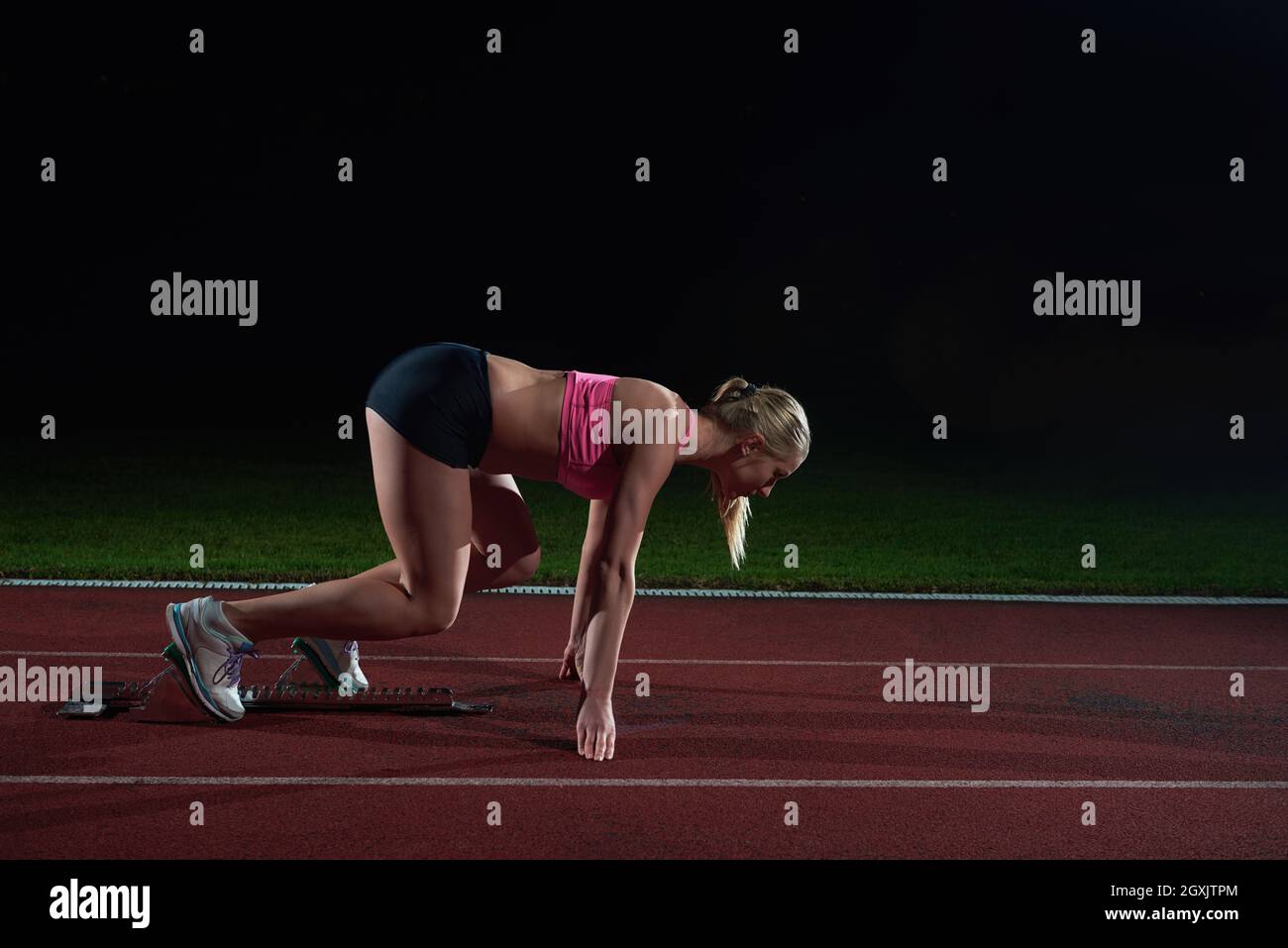 woman sprinter leaving starting blocks on the athletic track. Side view ...